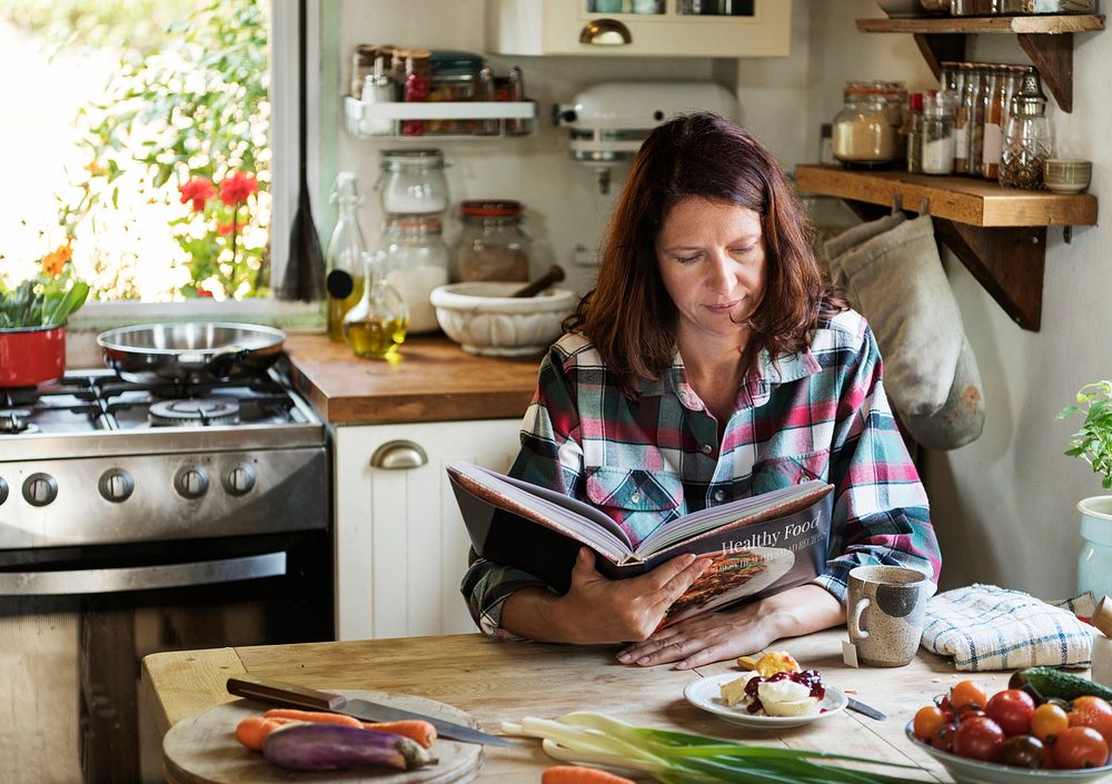 Woman reading a cookbook in the kitchen | Photo - rawpixel
