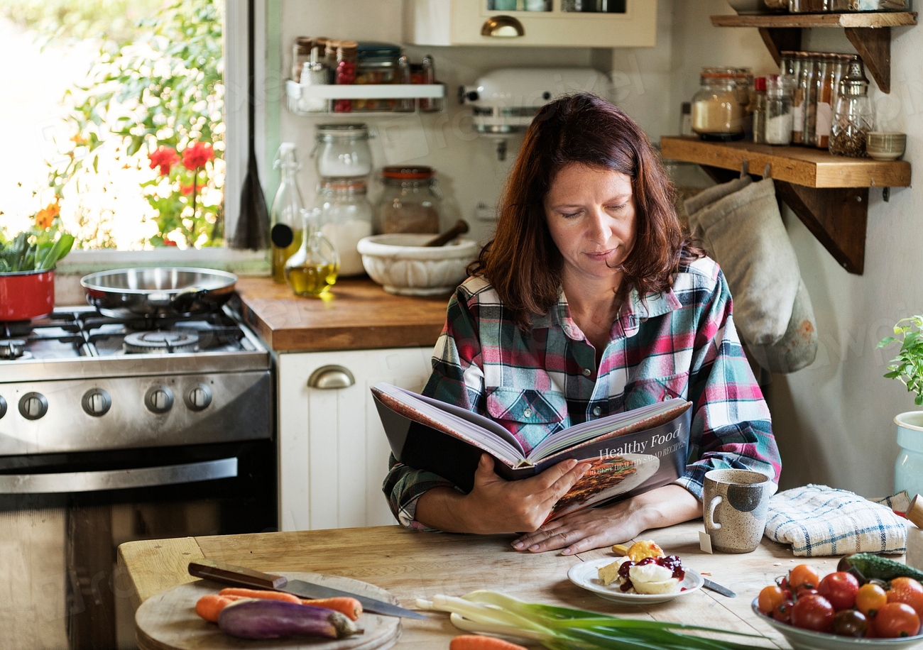 Woman reading a cookbook in the kitchen | Photo - rawpixel